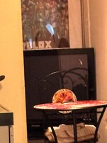 Mesa de jantar com uma pizza, uma cadeira e uma janela com um cartaz.