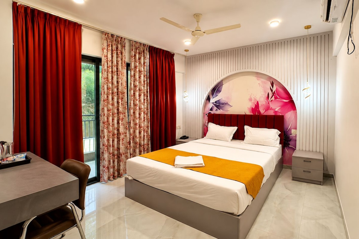 Quarto de hotel com cama, mesas de cabeceira, escrivaninha e janela com cortinas.
