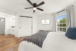 Um quarto com cama, ventilador de teto, janela com cortinas e banheiro com chuveiro e vaso sanitário.