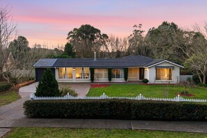 Uma casa de dois andares com telhado plano, painéis solares e um gramado bem cuidado.
