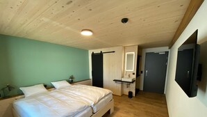 Quarto com cama, mesa de cabeceira, espelho, um pequeno armário e uma porta.