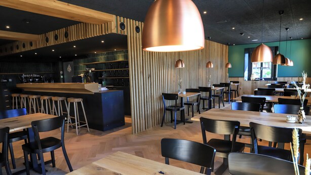 Interior moderno de restaurante com mobiliário de madeira, iluminação pendente e um bar.