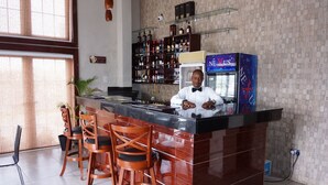 A bar area with a bartender, wooden chairs, a counter with a beverage dispenser, and shelves with bottles.