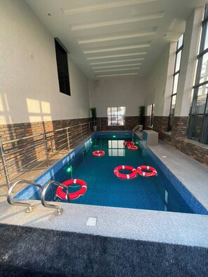 Uma piscina interna com água cristalina, boias de segurança e chão revestido de azulejos.