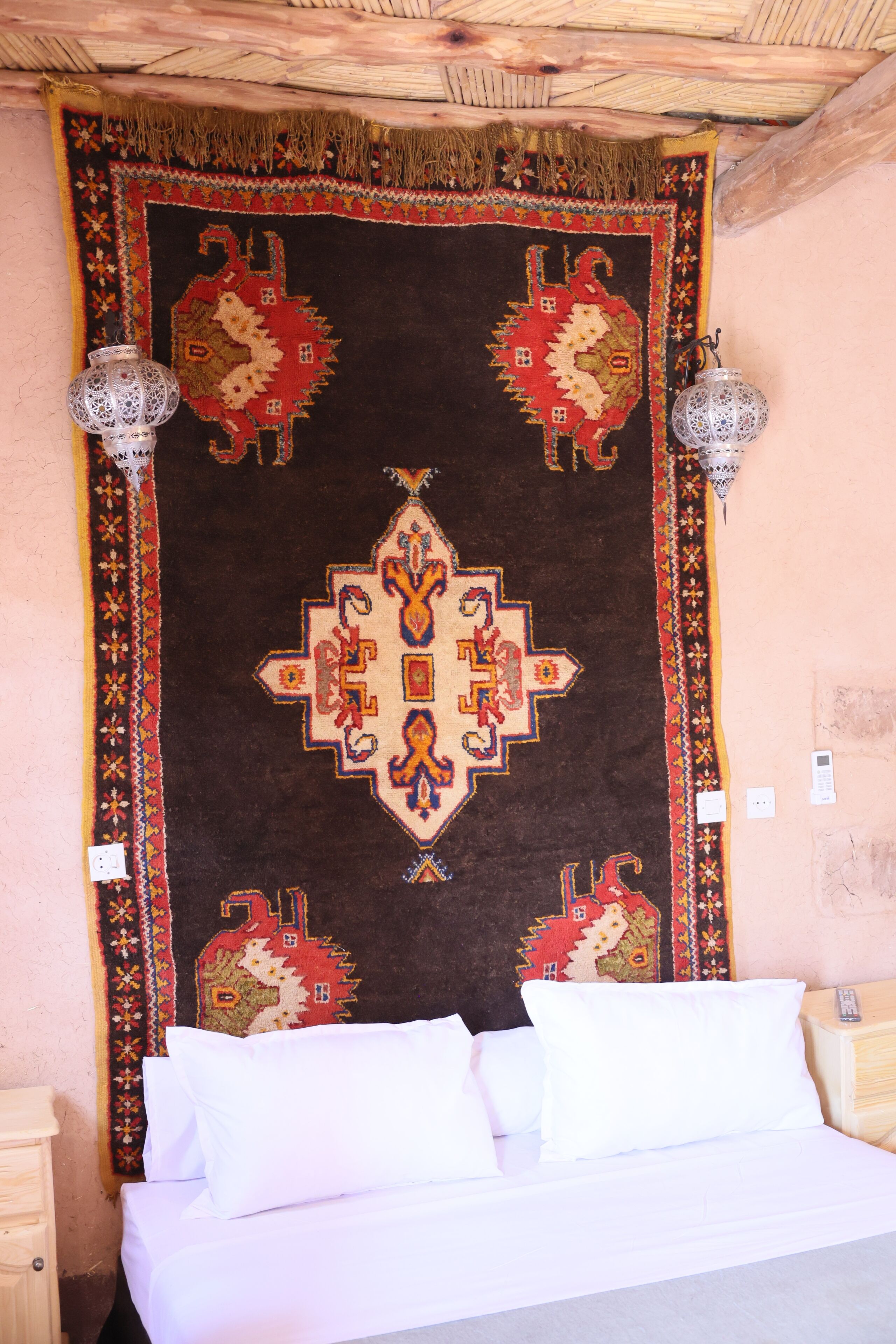 Um quarto com uma cama, um tapeçário de parede e duas luminárias fixadas na parede.