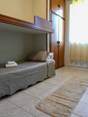 Uma cama de solteiro com colcha, cabeceira de madeira, uma porta e uma janela com cortinas.