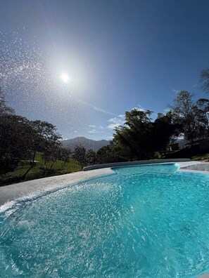 Uma piscina com água azul cristalina, cercada por árvores e uma montanha ao fundo.