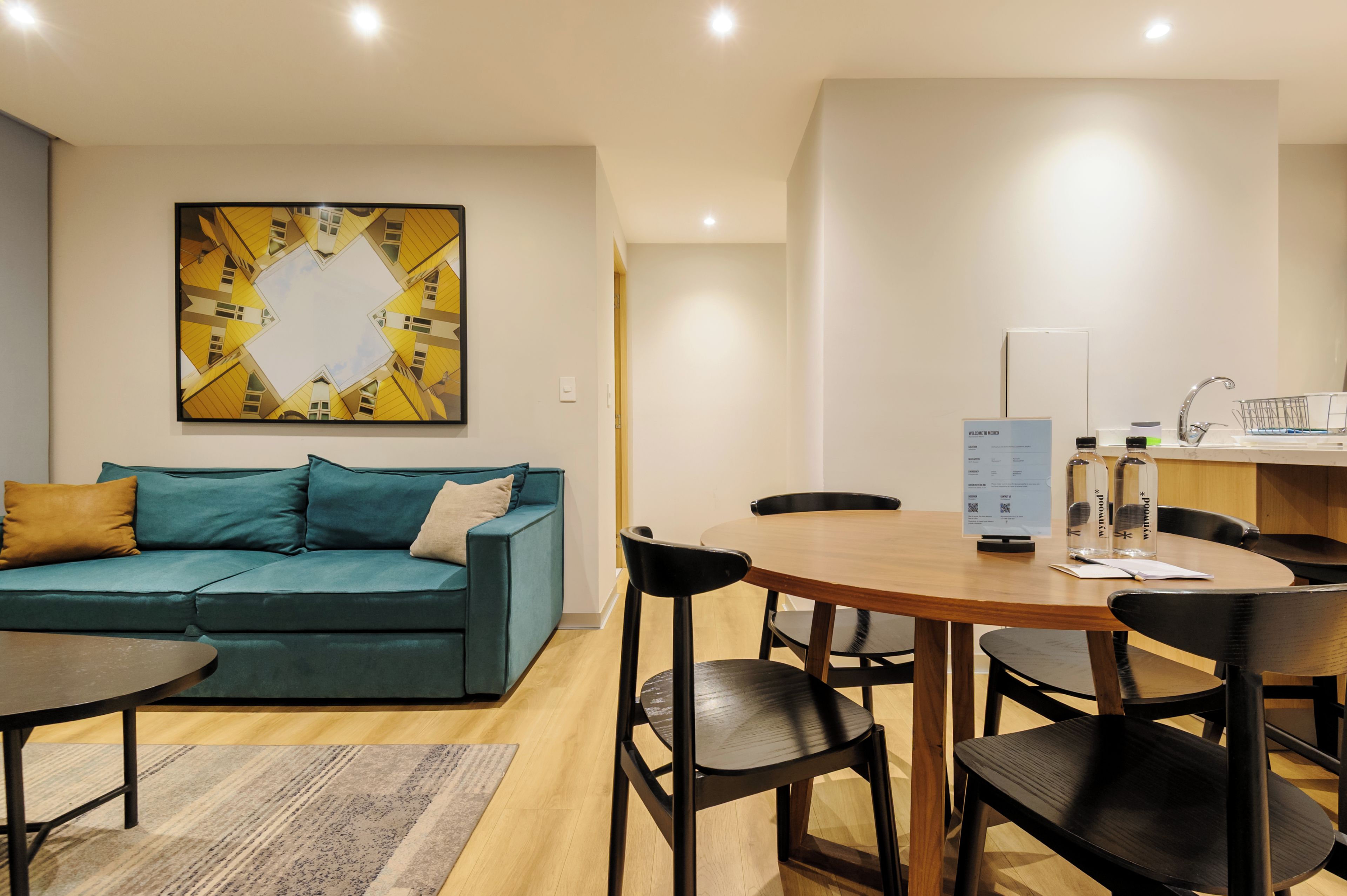 Uma sala de estar moderna com um sofá azul-turquesa, uma mesa de jantar de madeira com cadeiras, uma mesa de centro e um grande quadro abstrato na parede.