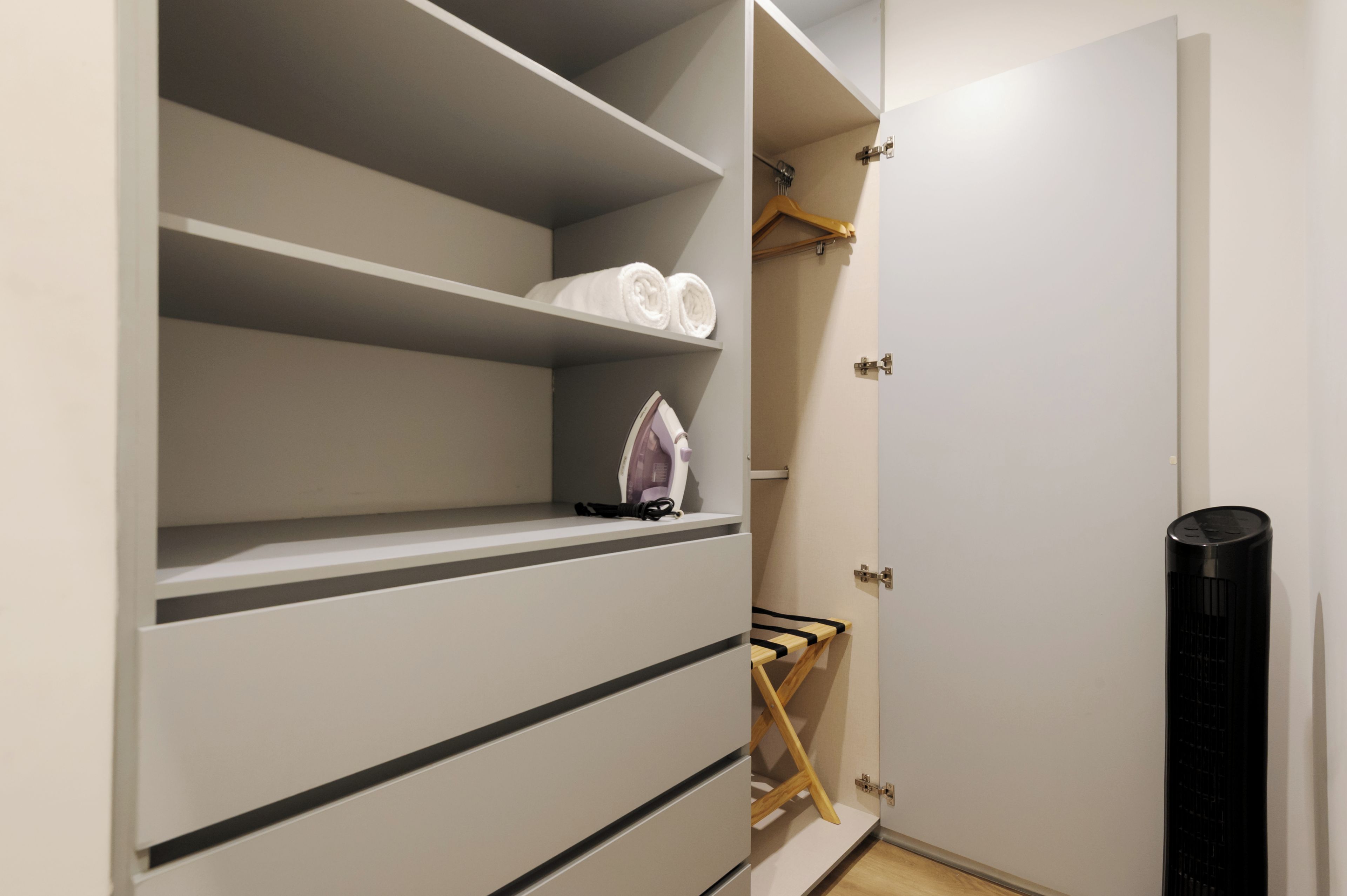 Um closet amplo com prateleiras abertas, cabideiro e um ferro pequeno.