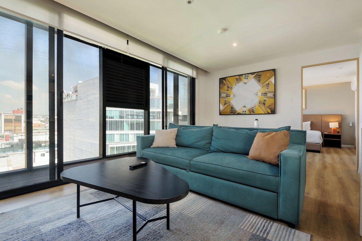 Uma sala de estar moderna com um sofá verde-água, uma mesa de centro preta e uma janela grande com vista para a cidade.