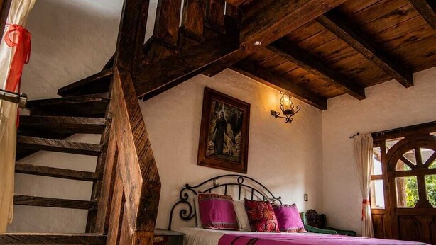 Um quarto com escada de madeira, cama com roupa de cama rosa e um quadro na parede.