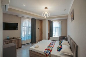 Quarto de hotel com uma cama, uma escrivaninha, uma cadeira, uma televisão e um candeeiro de teto.