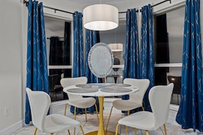 Uma sala de jantar com uma mesa redonda, cadeiras brancas e um espelho decorativo central.