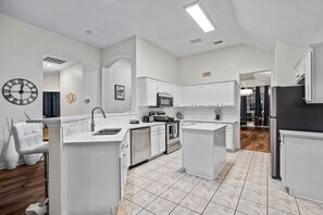 Uma cozinha moderna com armários brancos, uma pia de aço inoxidável e piso revestido de azulejos.