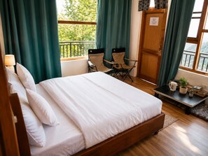 Quarto com cama, uma cadeira, uma mesa pequena com objetos e vista para o verde lá fora.