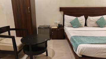 Quarto de hotel com cama, mesa de cabeceira, cadeira e pequena escrivaninha com telefone.