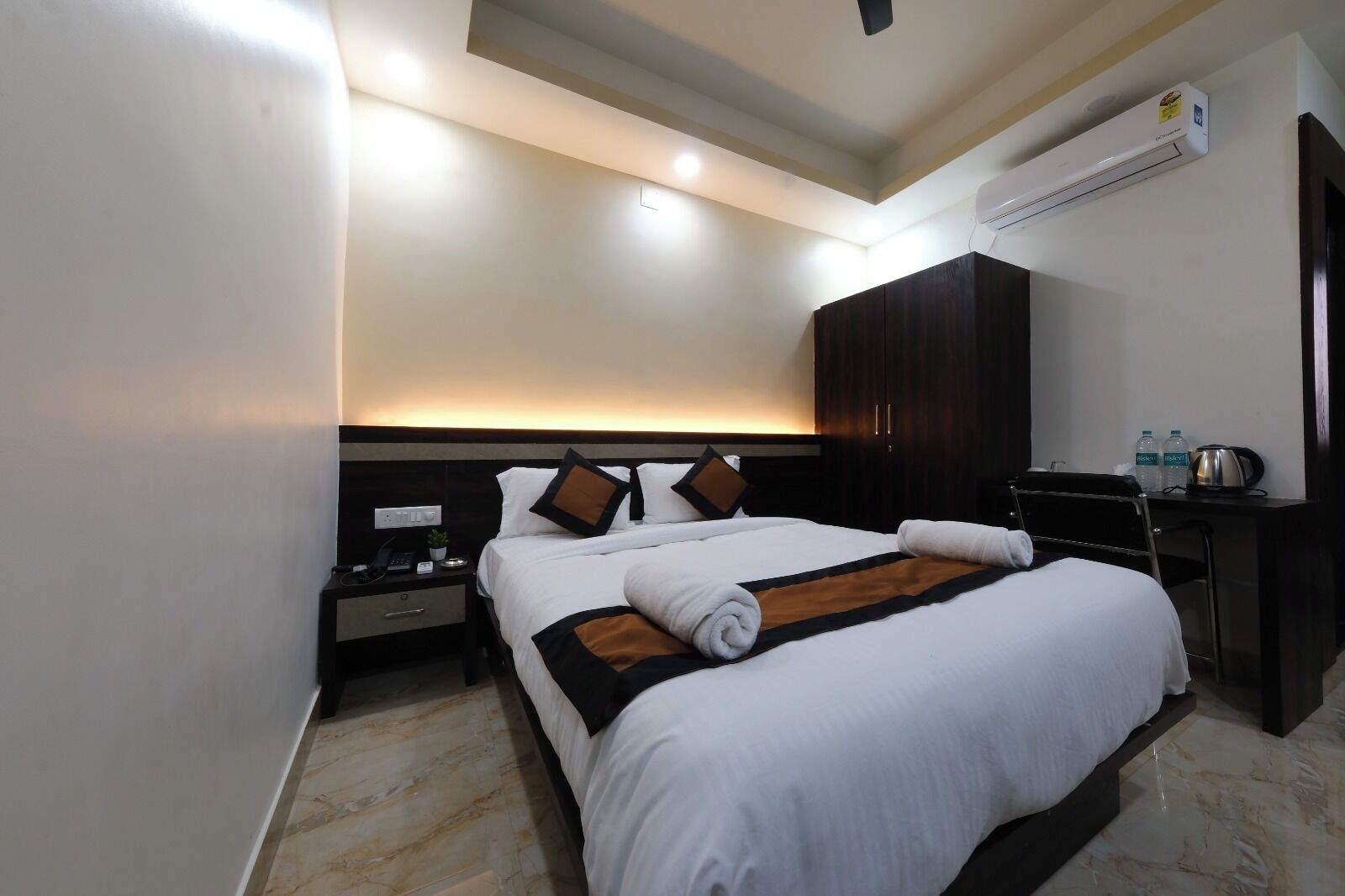 Quarto de hotel com uma cama grande, uma mesa de cabeceira com abajur, um guarda-roupa e um aparelho de ar condicionado.