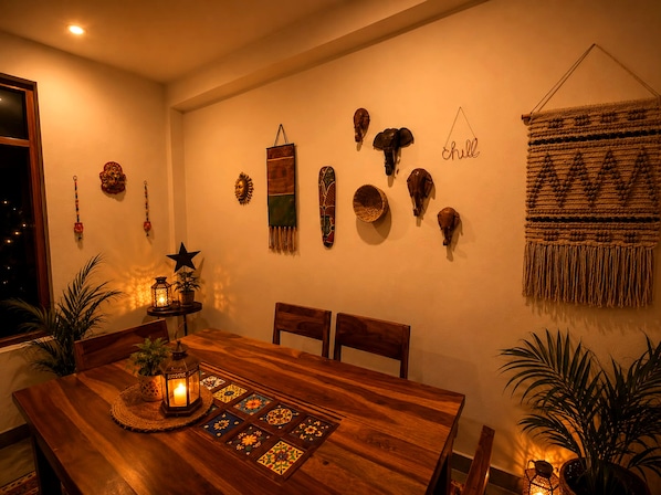 Uma área de refeições com uma mesa de madeira, cadeiras, uma parede decorativa com diversos objetos e uma peça de macramé pendurada.