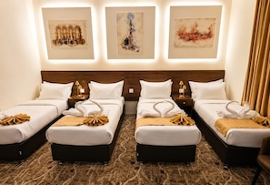 Quarto de hotel com duas camas, cabeceira, obras de arte na parede e piso coberto por carpete.