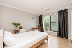 Quarto com cama, mesa de cabeceira, planta, escrivaninha e janela com cortinas.