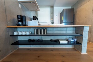 Cozinha compacta com cafeteira, canecas de aço inoxidável e geladeira.