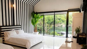 Quarto moderno com uma cama grande, uma escrivaninha e vista para um lago através de janelas do chão ao teto.