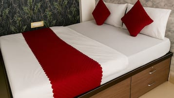 Uma cama com colchão branco, manta vermelha e duas almofadas vermelhas.