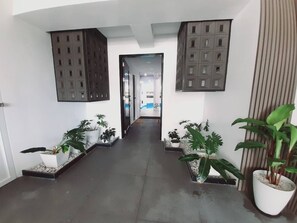 Um corredor com plantas em vasos, vista para outro ambiente e uma grande janela com persianas.