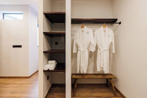 Um closet espaçoso com prateleiras de madeira, um banco e dois roupões brancos pendurados em ganchos.