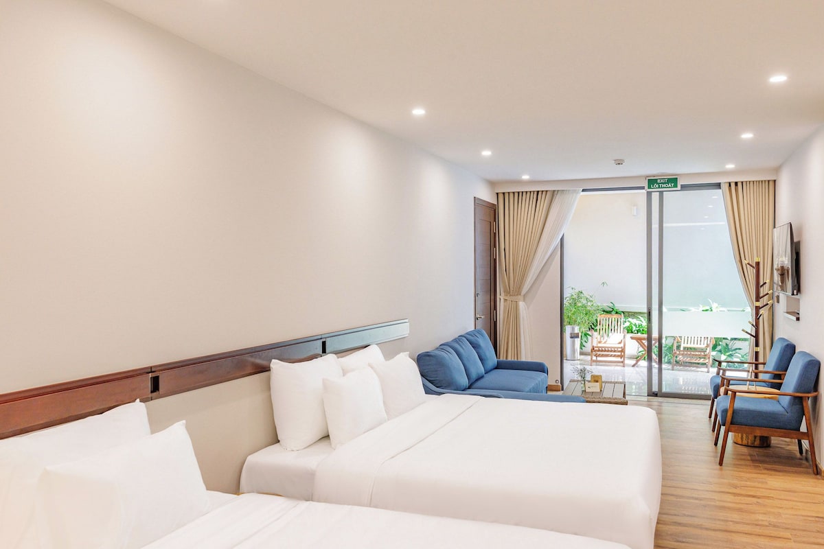 Quarto de hotel com duas camas, varanda com área de estar e vista para o exterior.