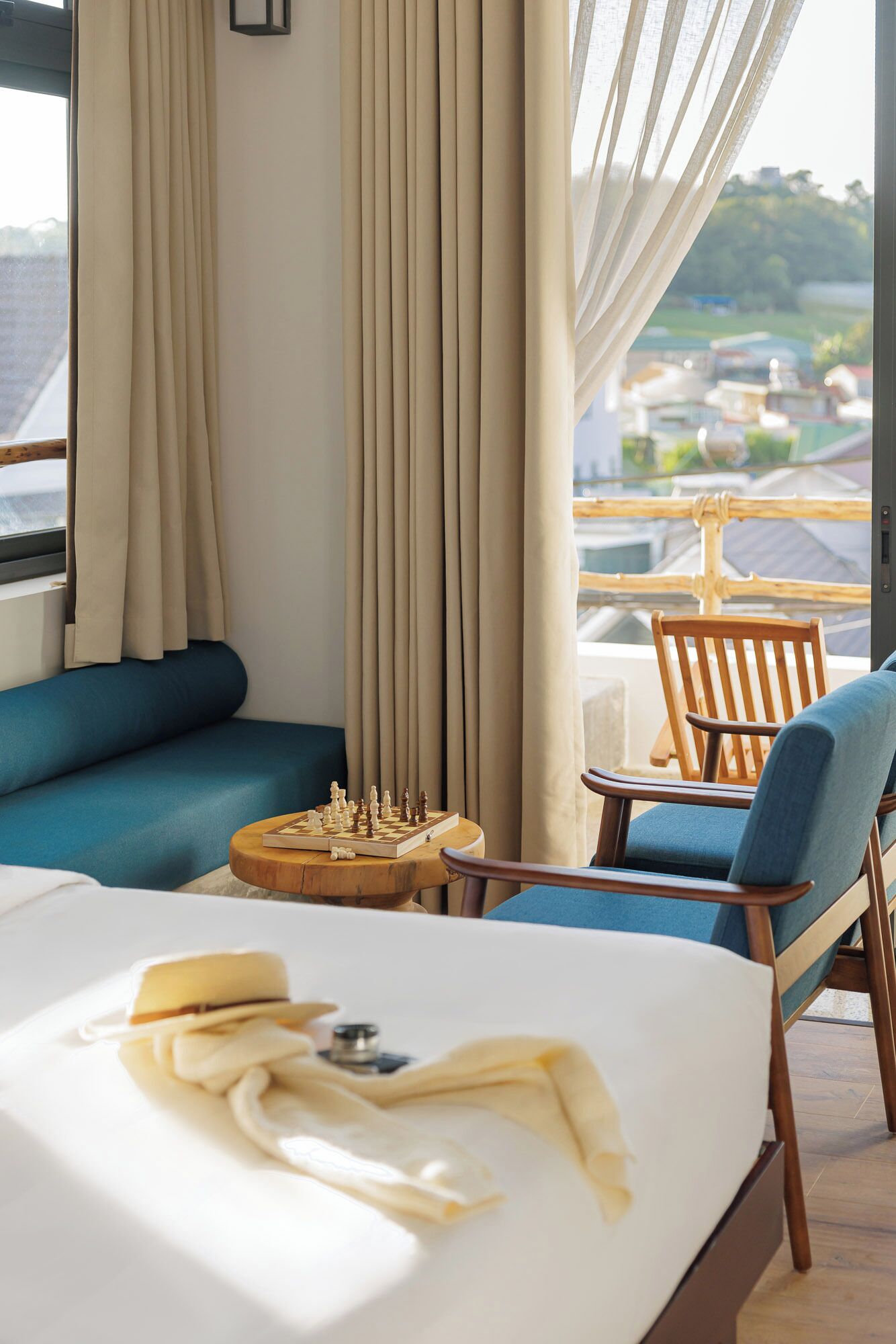 Quarto de hotel com cama, um tabuleiro de xadrez, uma mesa de jantar com uma cadeira e vista para a cidade através de amplas janelas.
