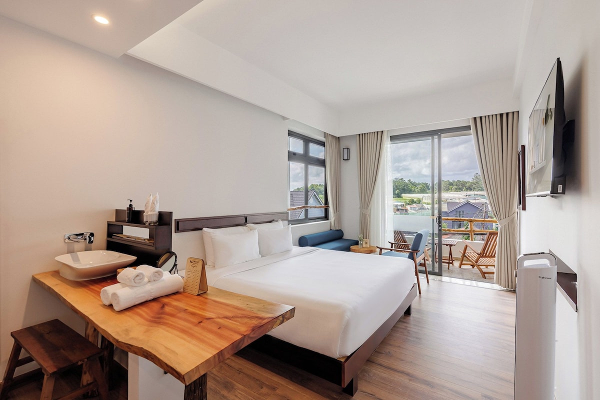 Quarto de hotel com cama, mesa de cabeceira e vista para o exterior.
