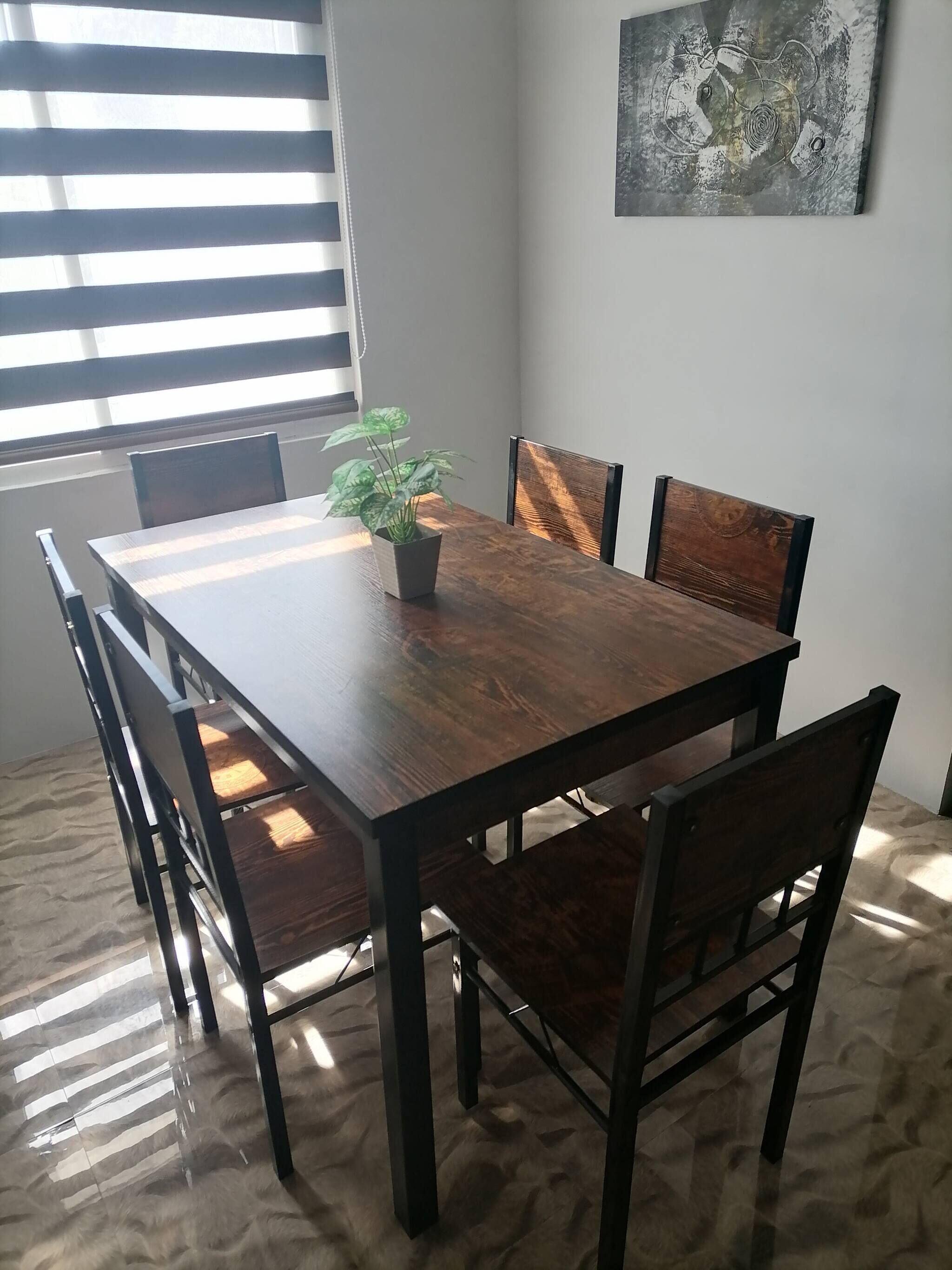 Uma mesa de jantar com cadeiras, um vaso de planta e um quadro na parede.