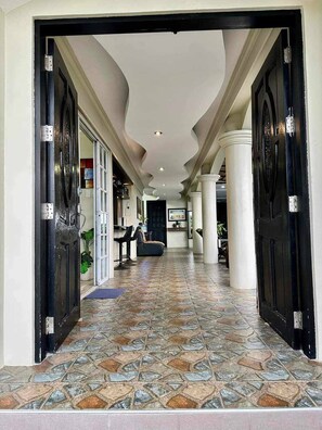 Um corredor com piso ladrilhado, portas pretas e colunas brancas.