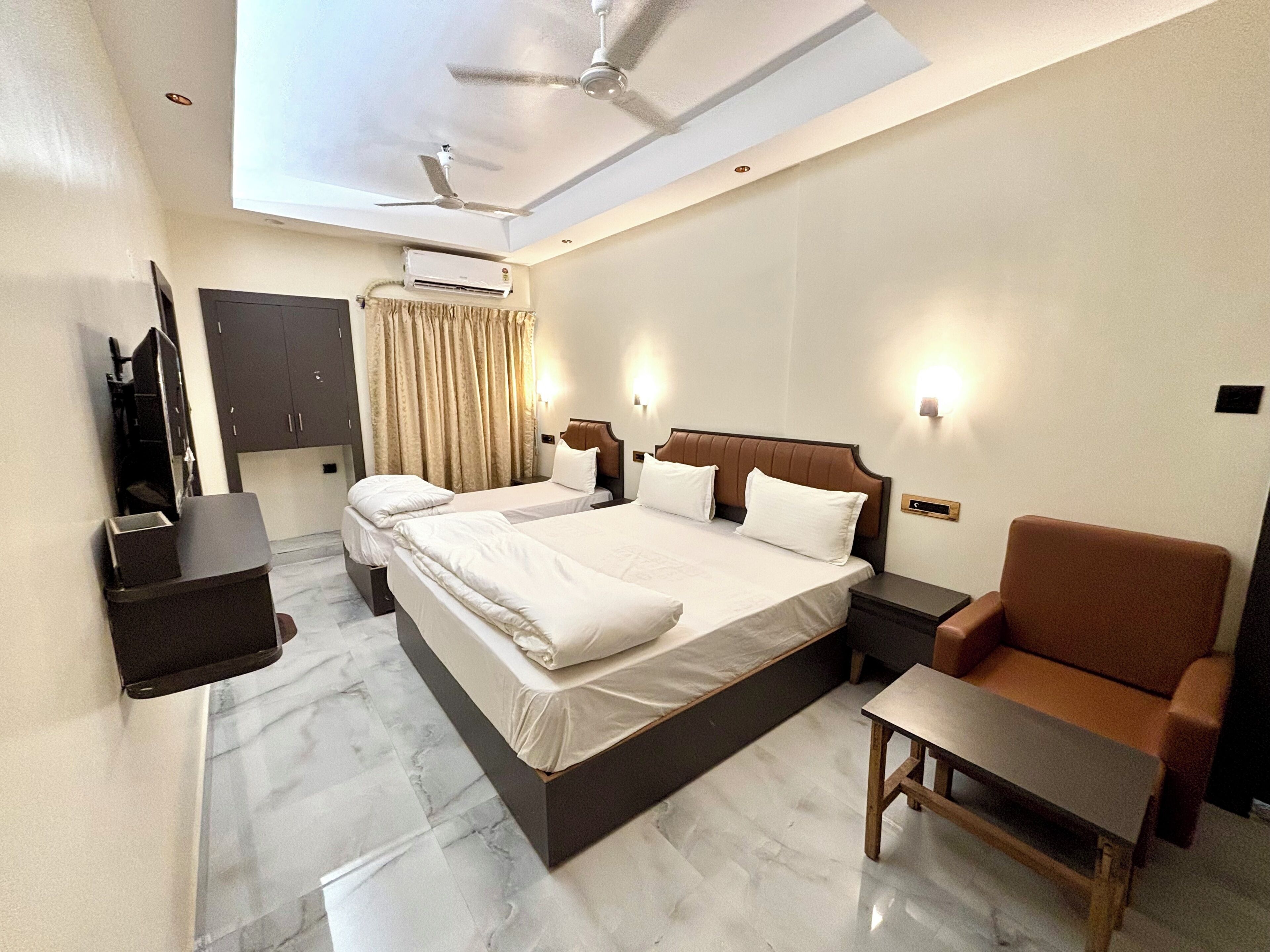 Quarto de hotel com cama, poltrona, mesa pequena, televisão e ar condicionado.