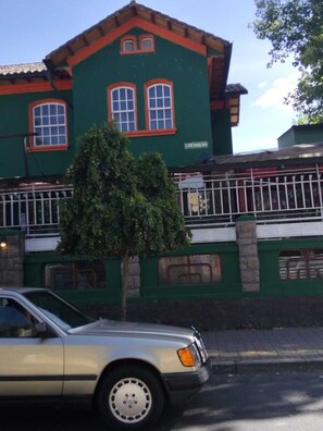 Um edifício com fachada verde, duas janelas com molduras vermelhas e uma árvore em frente.