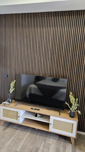 Uma televisão de tela plana em um móvel de madeira, com uma parede de ripas ao fundo.