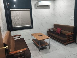 Uma sala de estar com sofá, uma mesa pequena e uma janela com padrão geométrico.