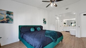 A bedroom with a bed, a ceiling fan, and a bathroom visible in the background.