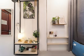 Um quarto com um espelho, uma luminária, prateleiras com livros e plantas, e uma porta com uma placa.