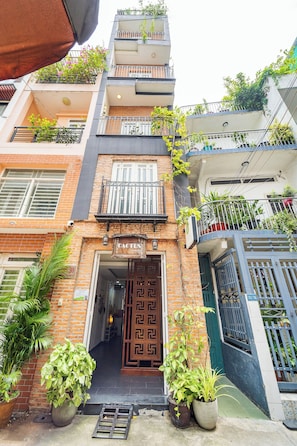 Um edifício de vários andares com uma entrada central, varandas com plantas e uma entrada no andar térreo.