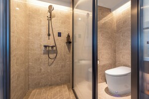 Uma casa de banho moderna com chuveiro em cabine de vidro, sanita e lavatório com artigos de higiene pessoal.