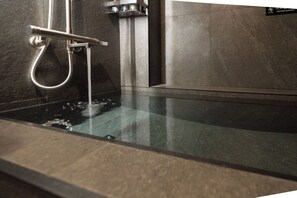 Uma casa de banho moderna com banheira separada por vidro, chuveiro manual e um sinal de aviso na parede.