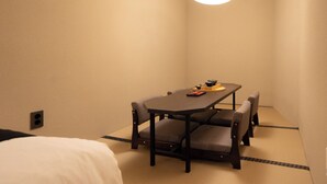 A small, private room with a single table and four chairs, a bed, and a wall-mounted light fixture.