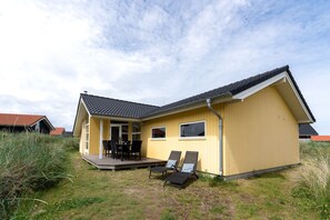 Um edifício amarelo com um alpendre coberto e duas cadeiras de descanso.