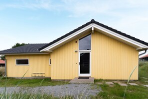 Um edifício térreo amarelo com telhado preto, uma pequena janela e uma porta.
