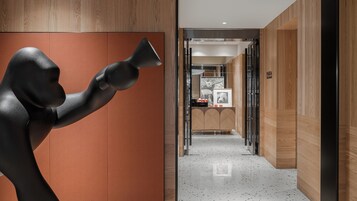 Um interior moderno com painel de madeira, uma escultura abstrata preta e um corredor que leva a um espaço com balcão e quadros emoldurados.