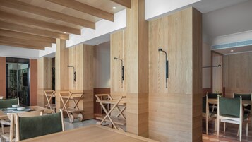 Um interior moderno com painéis de madeira, área de jantar com cadeiras estofadas em verde e teto aparente com vigas de madeira.