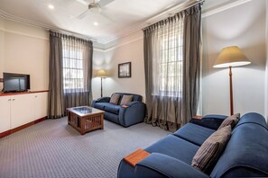 Uma sala de estar com sofá, mesa de centro, televisão e cortinas.