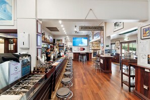 Uma área de bar com banquetas, balcão e uma tela de televisão.